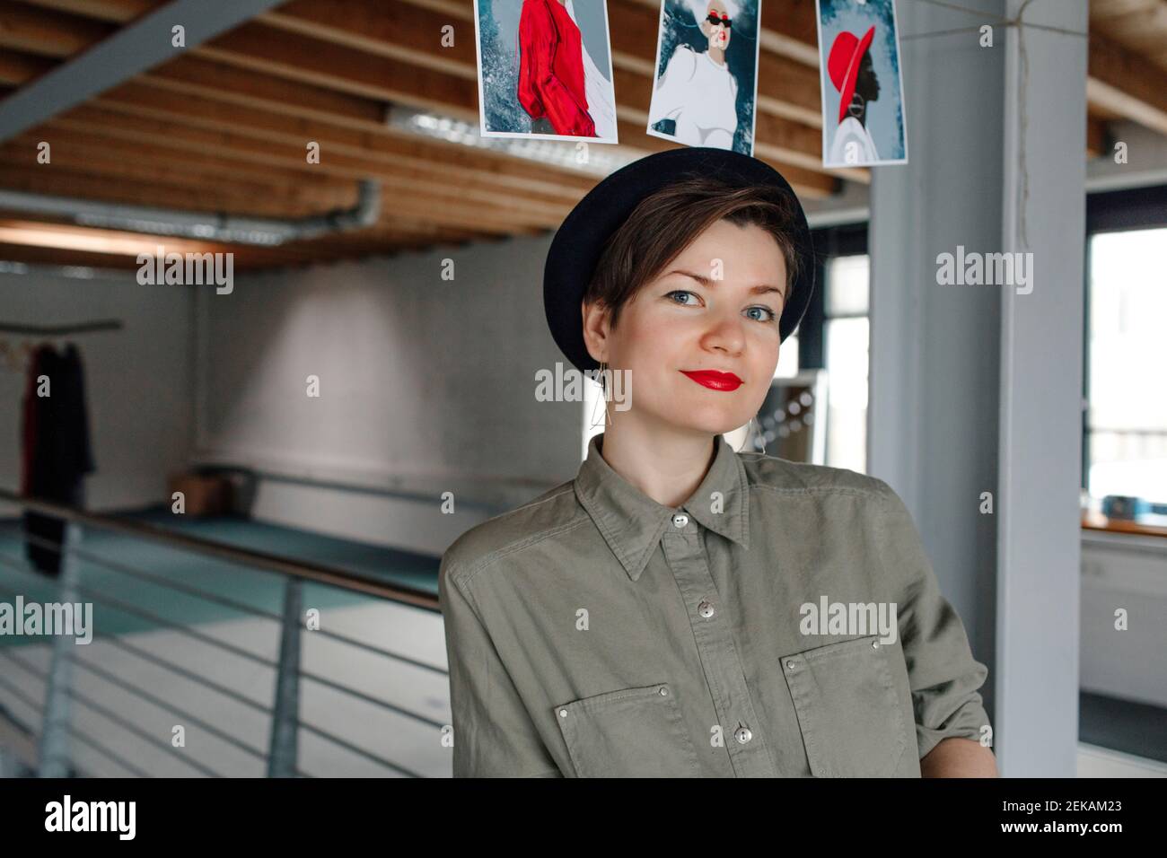Confident woman wearing hat staring while standing under painted image ...