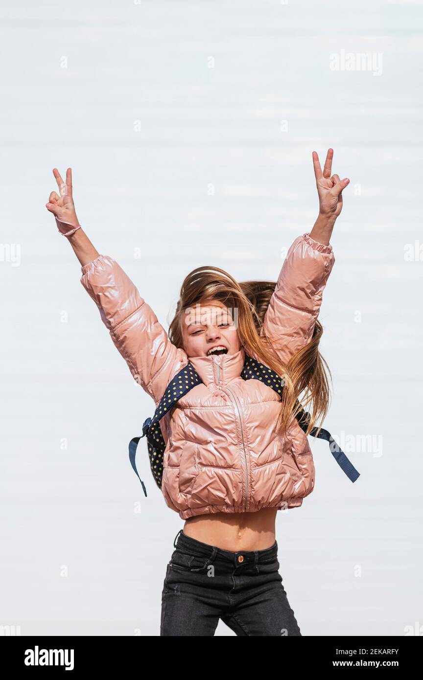 Laughing girl showing Peace sign while jumping in front of wall Stock ...