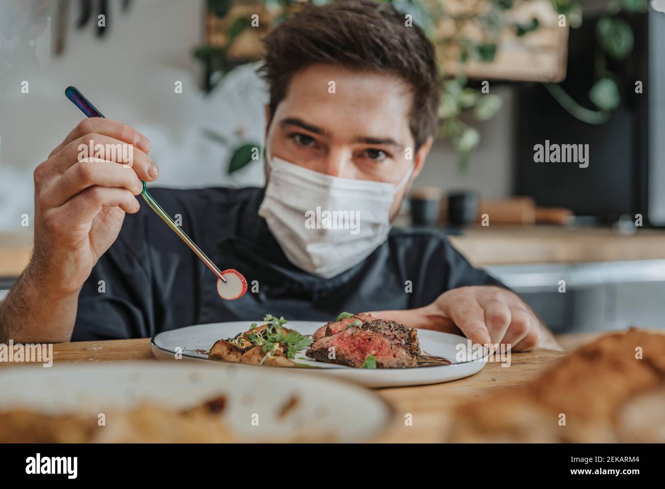 Male chef wearing protective face mask garnishing vegetable on tomahawk ...