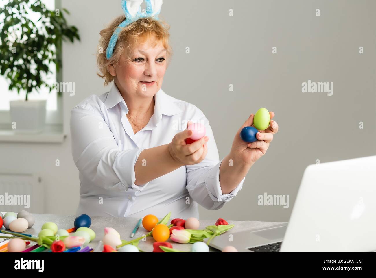 Beautiful senior woman with easter eggs and easter breads on the table ...