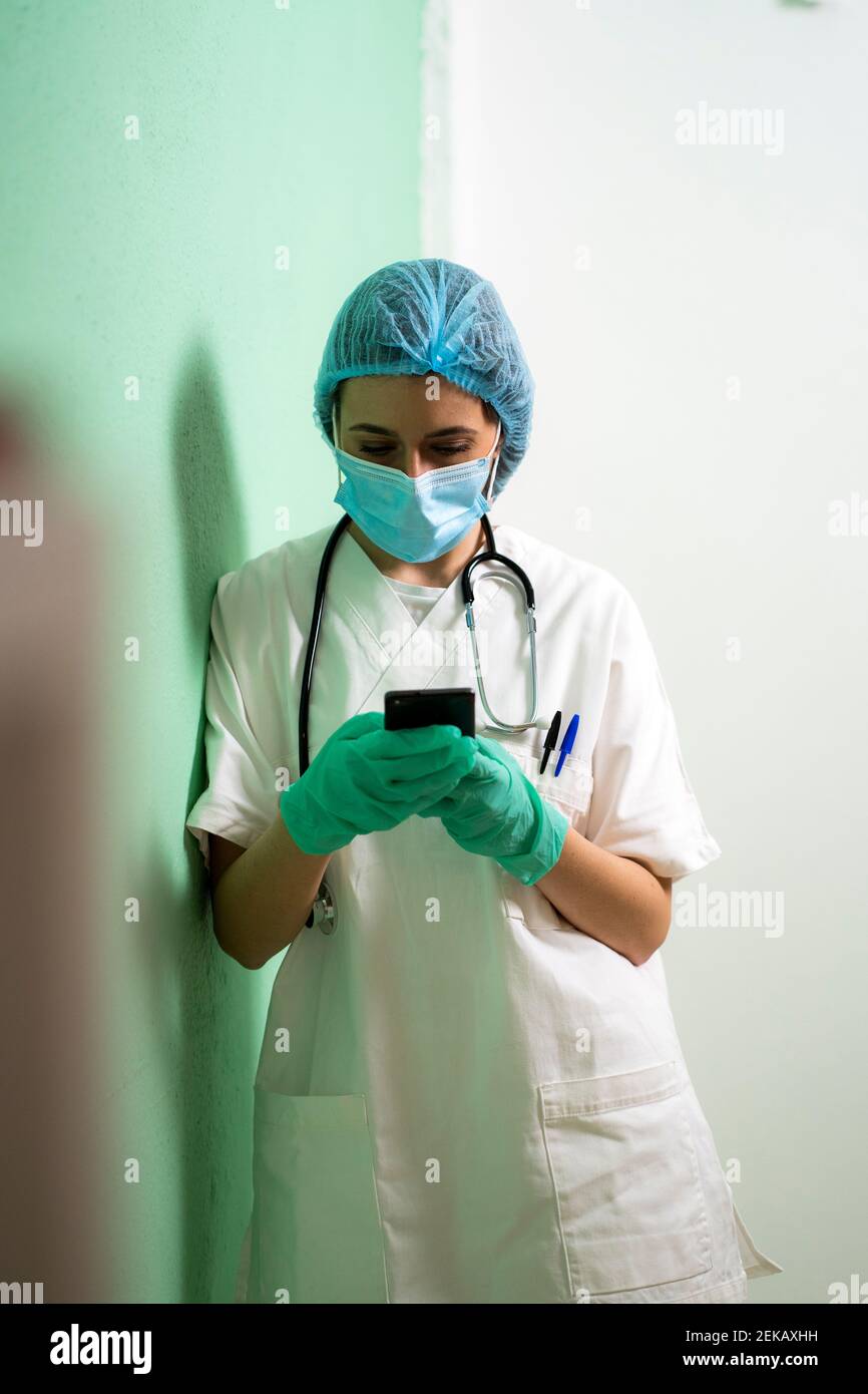 Female doctor using smart phone while leaning by wall at clinic Stock ...