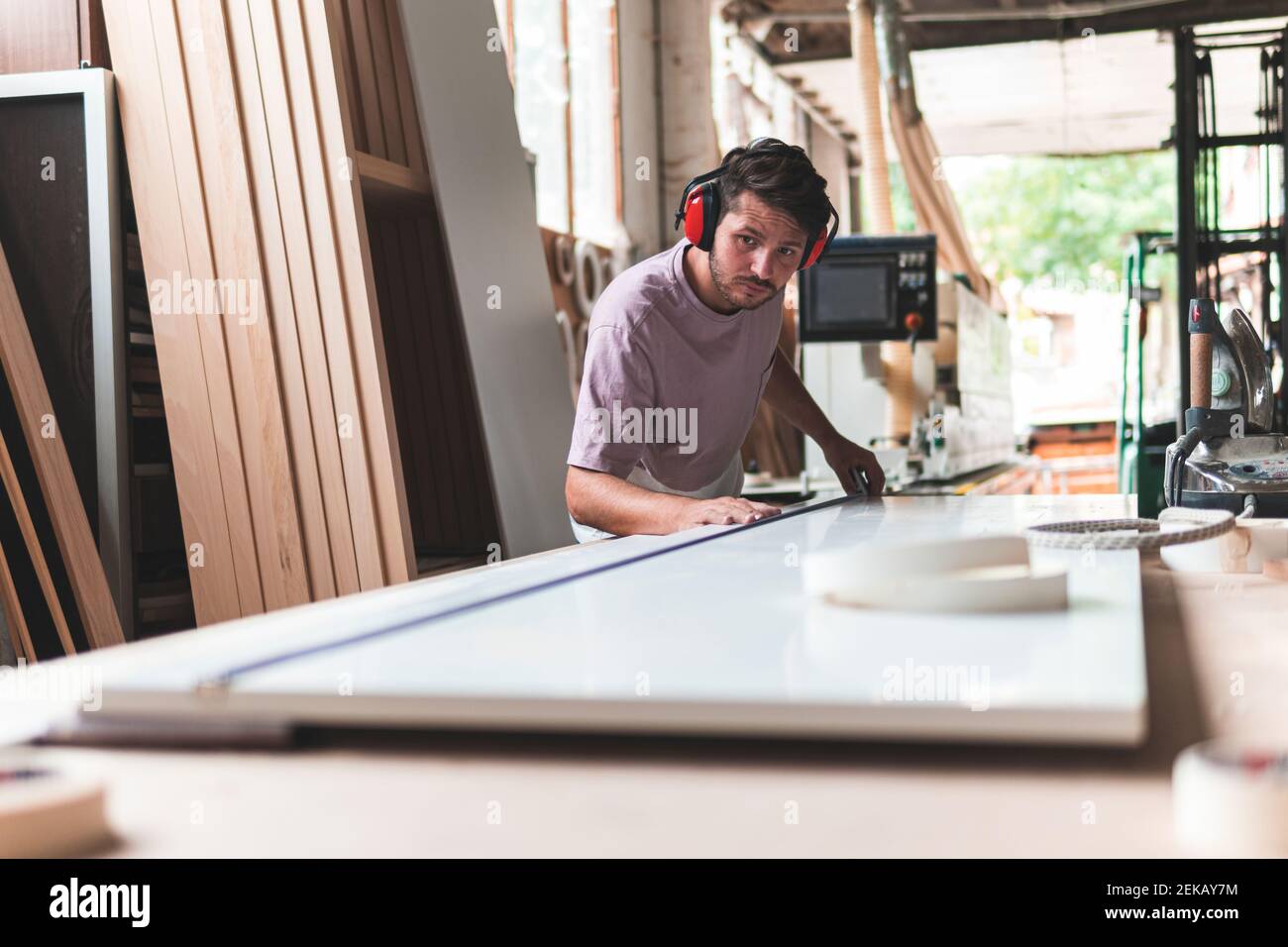 Male carpenter measuring plank using tape measure on workbench in ...