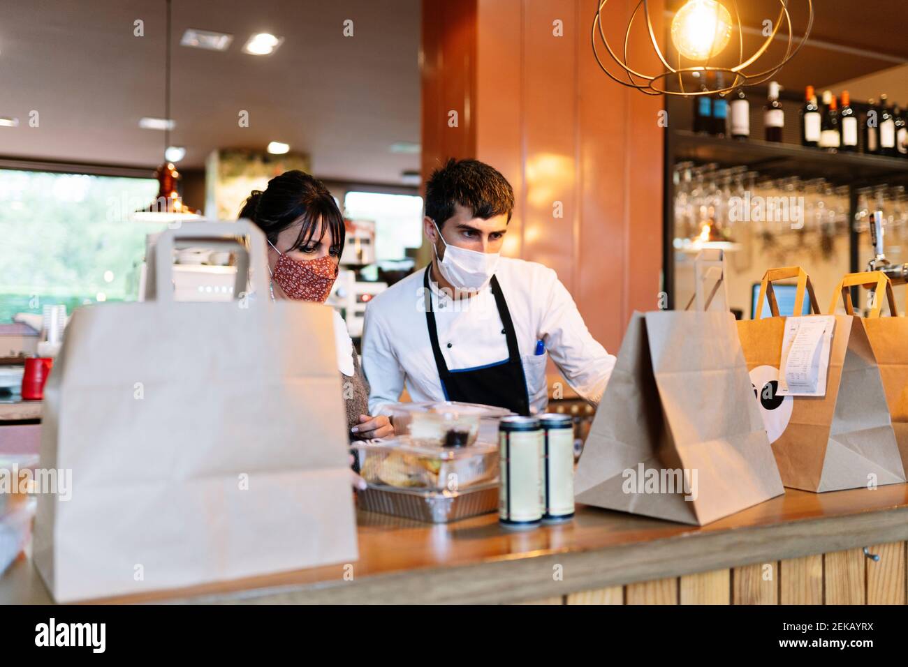 Female owner and male chef checking take out food orders on bar counter ...