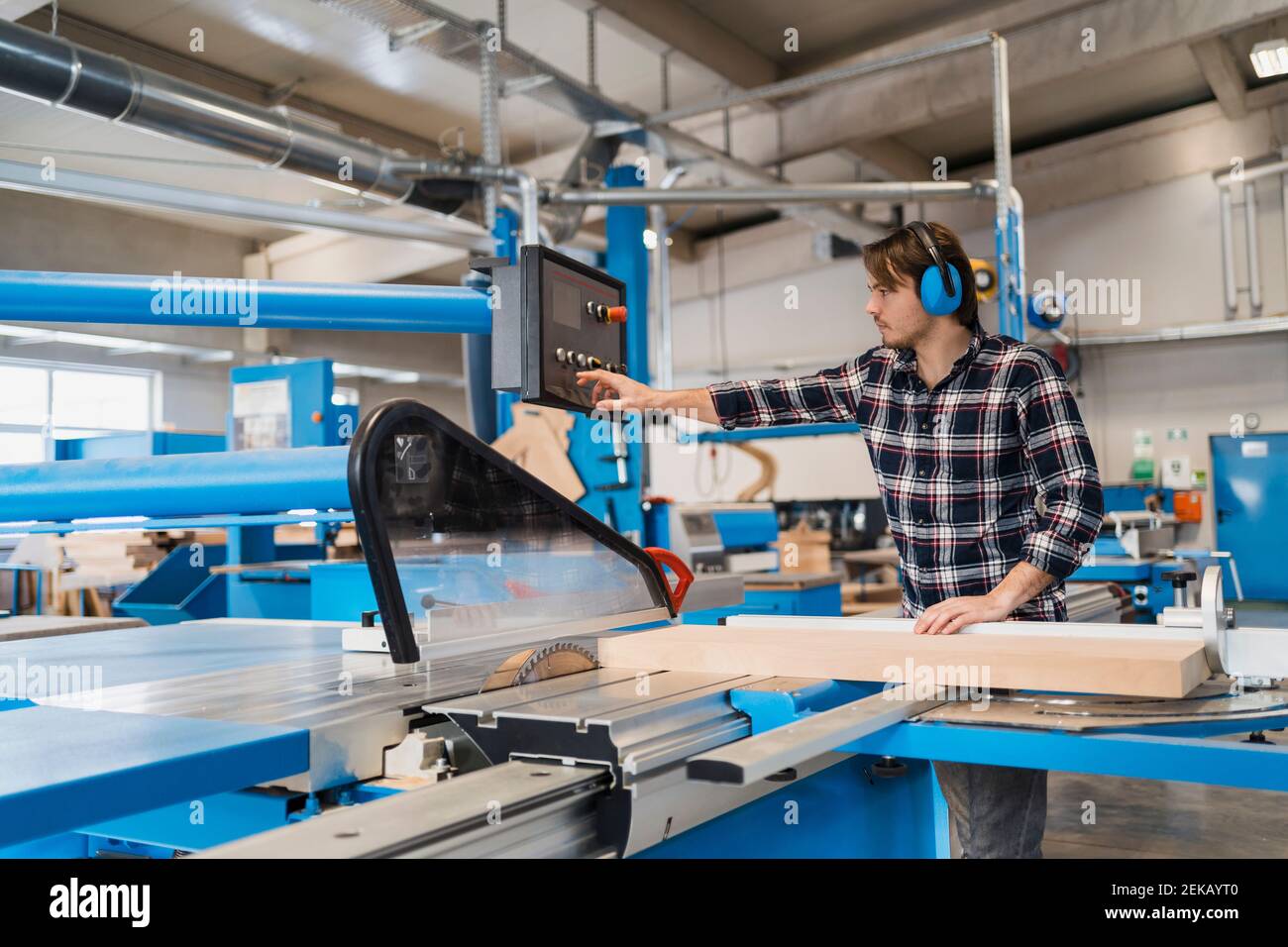 Male manual worker wearing ear muff operating machine while standing at ...