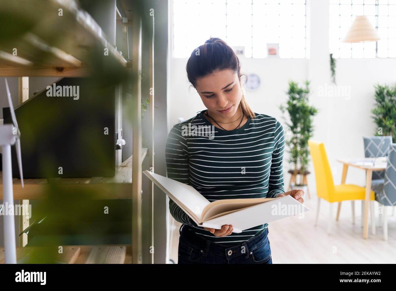 Female professional reading book while standing by bookshelf in office ...