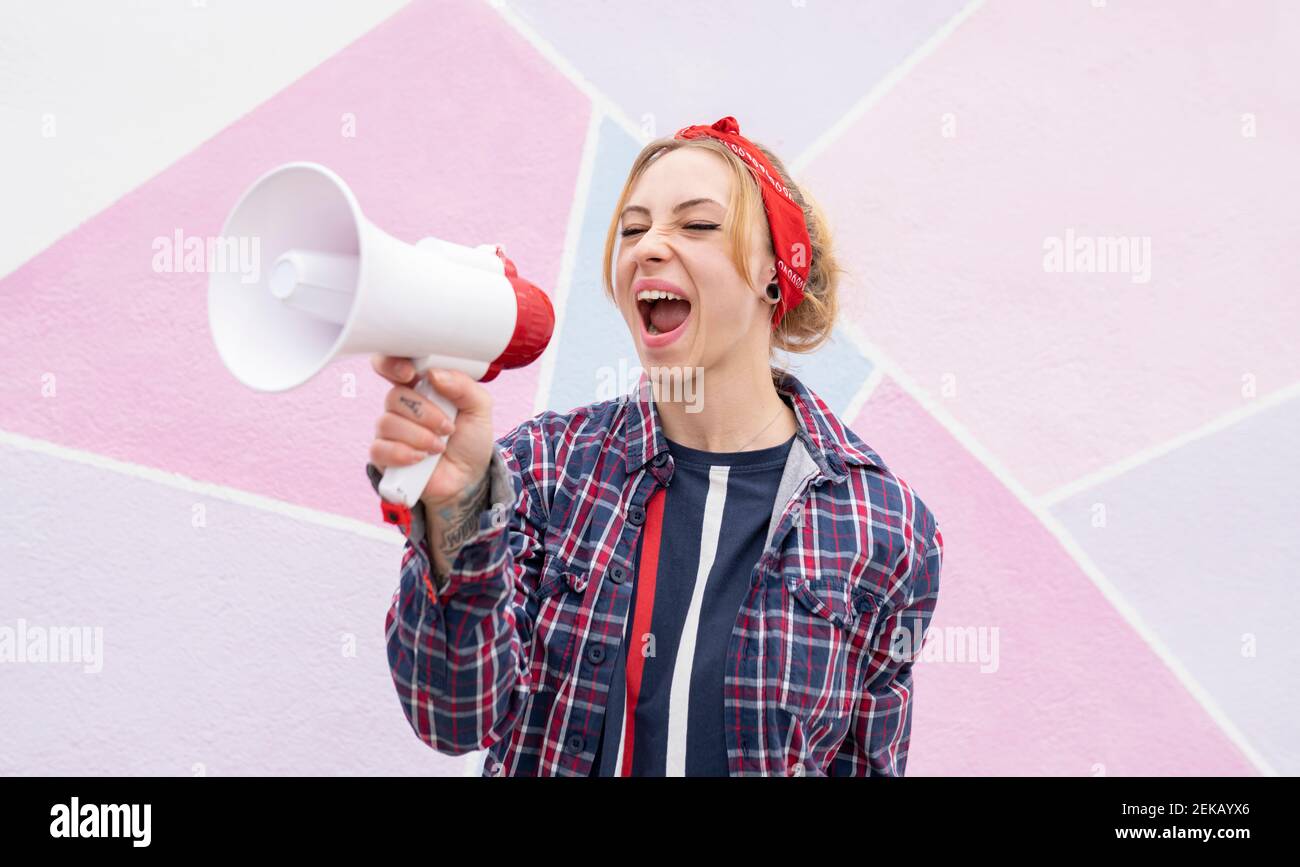 Woman screaming on megaphone while standing against wall Stock Photo ...