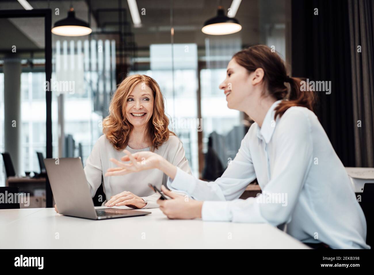 Businesswoman laughing while discussing with female colleague during ...