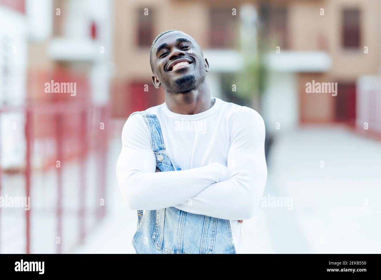 Happy young man in bib overalls standing with arms crossed Stock Photo ...