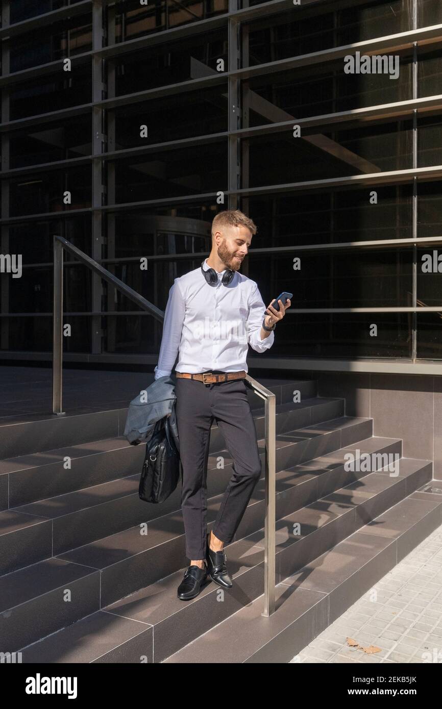 Mid adult businessman using mobile phone while standing on steps Stock ...