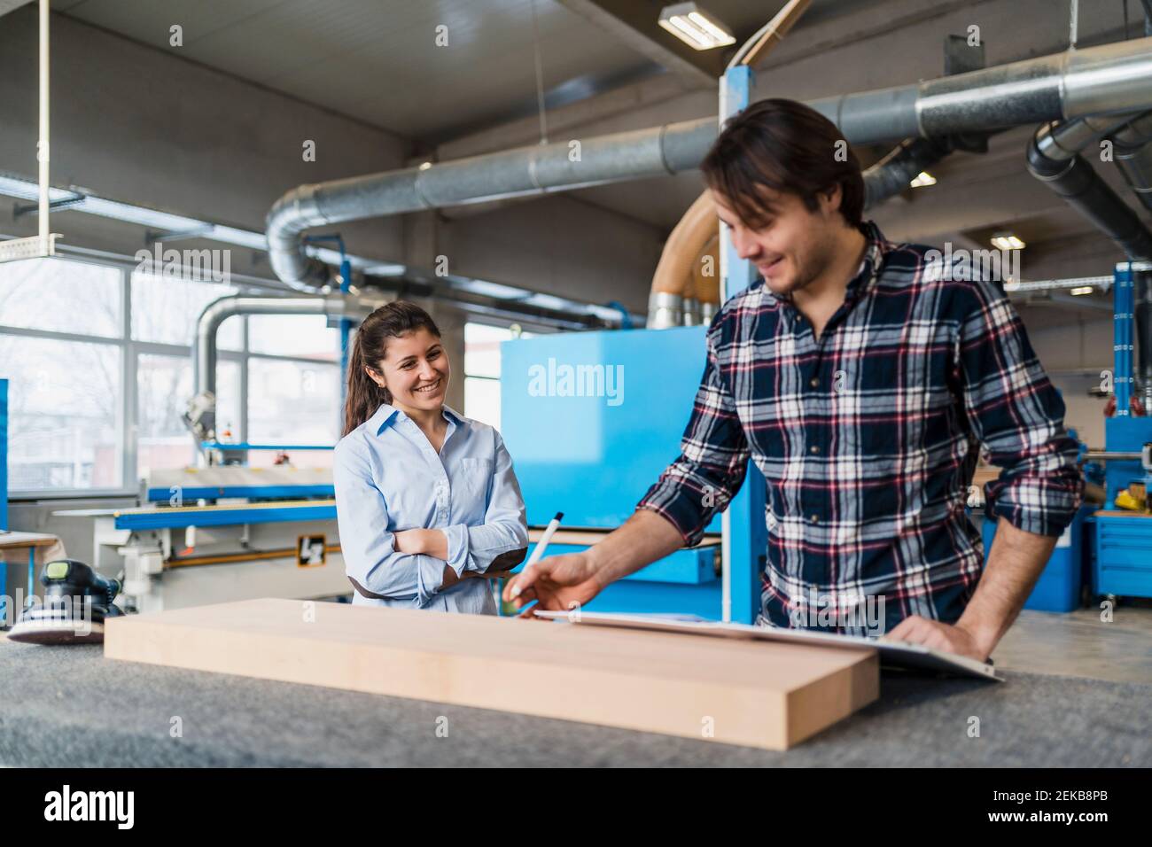 Manual worker measuring wood while standing by colleague at industry ...