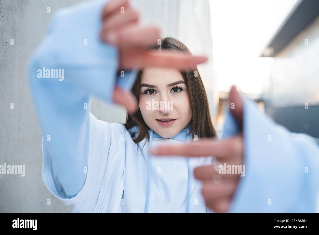 Young woman making finger frame while standing against wall Stock Photo ...