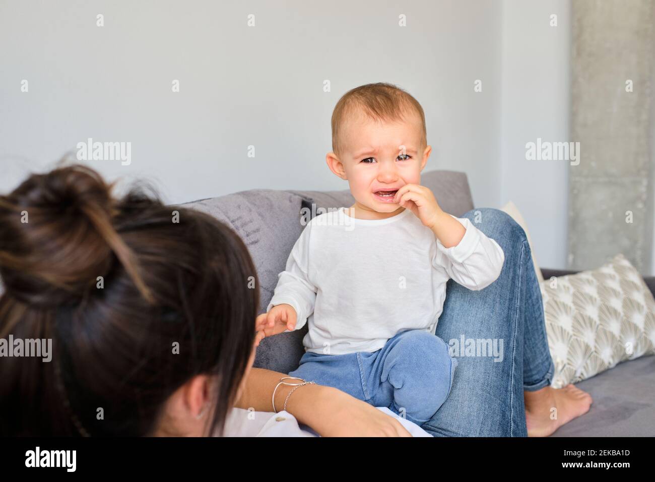 Baby girl grimacing while playing with mother on sofa Stock Photo - Alamy