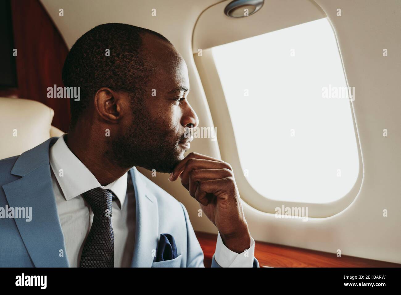 Male entrepreneur with hand on chin looking through window in airplane ...