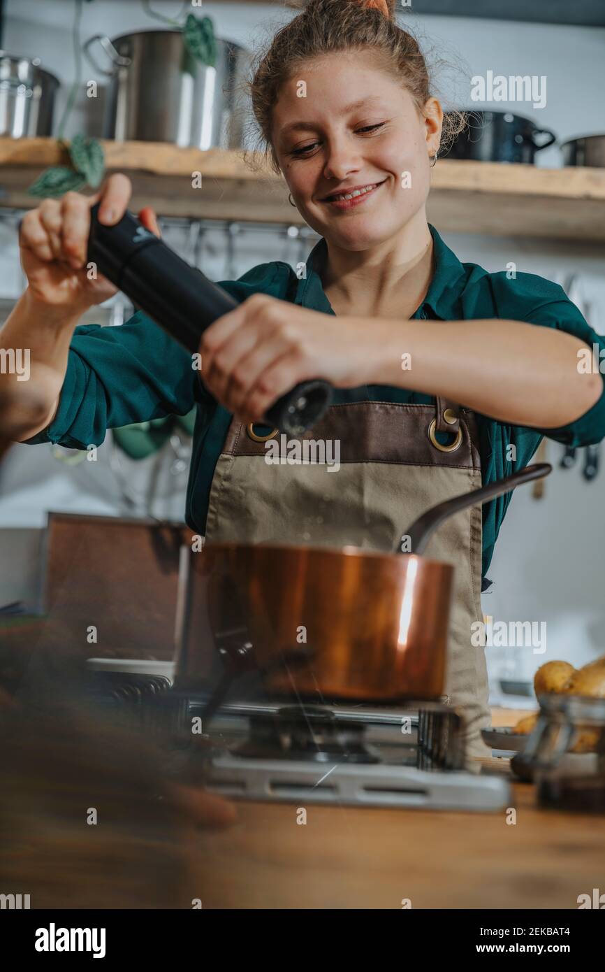 Smiling chef adding pepper in food while cooking in kitchen Stock Photo ...