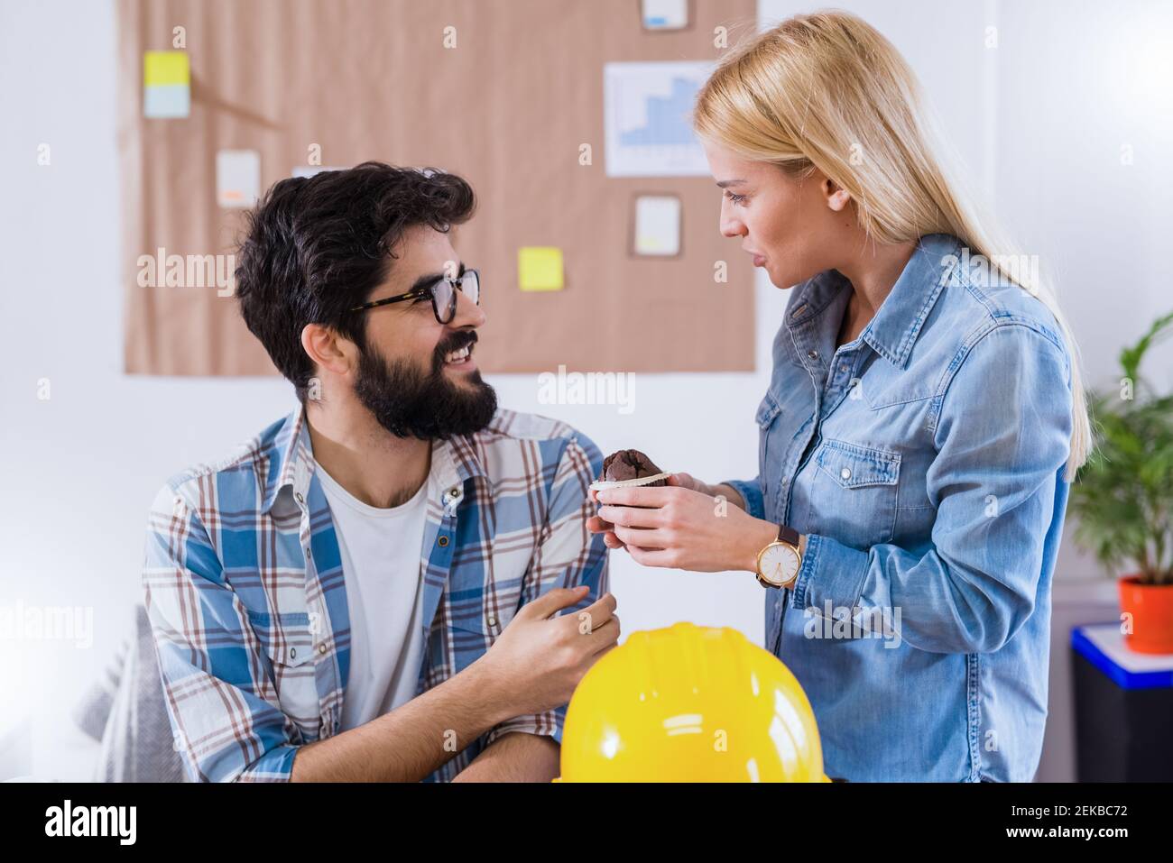 Two happy young colleagues sharing cookie on coffee break in their ...