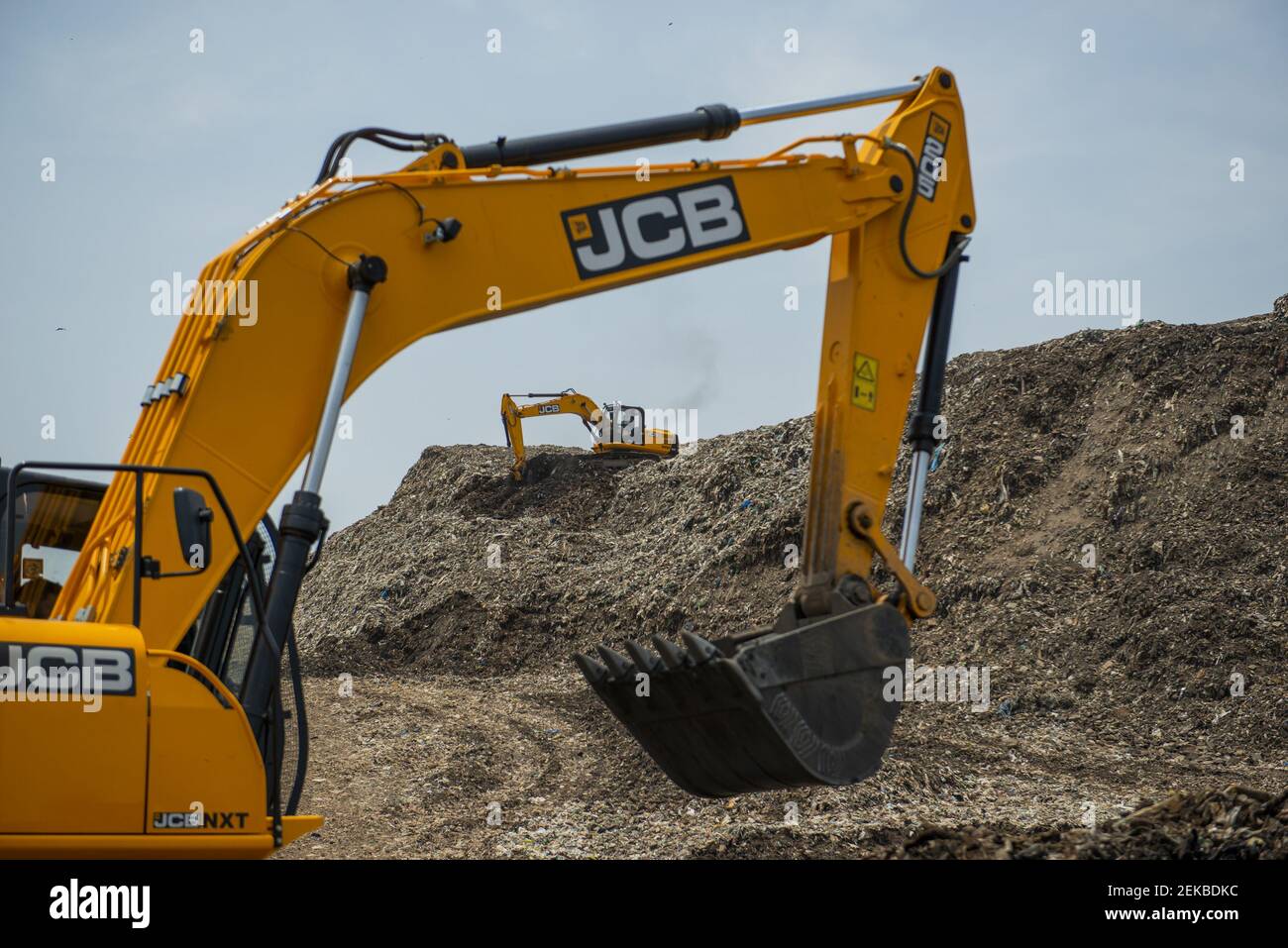 A JCB machine picking up waste in the pile of garbage. Waste ...