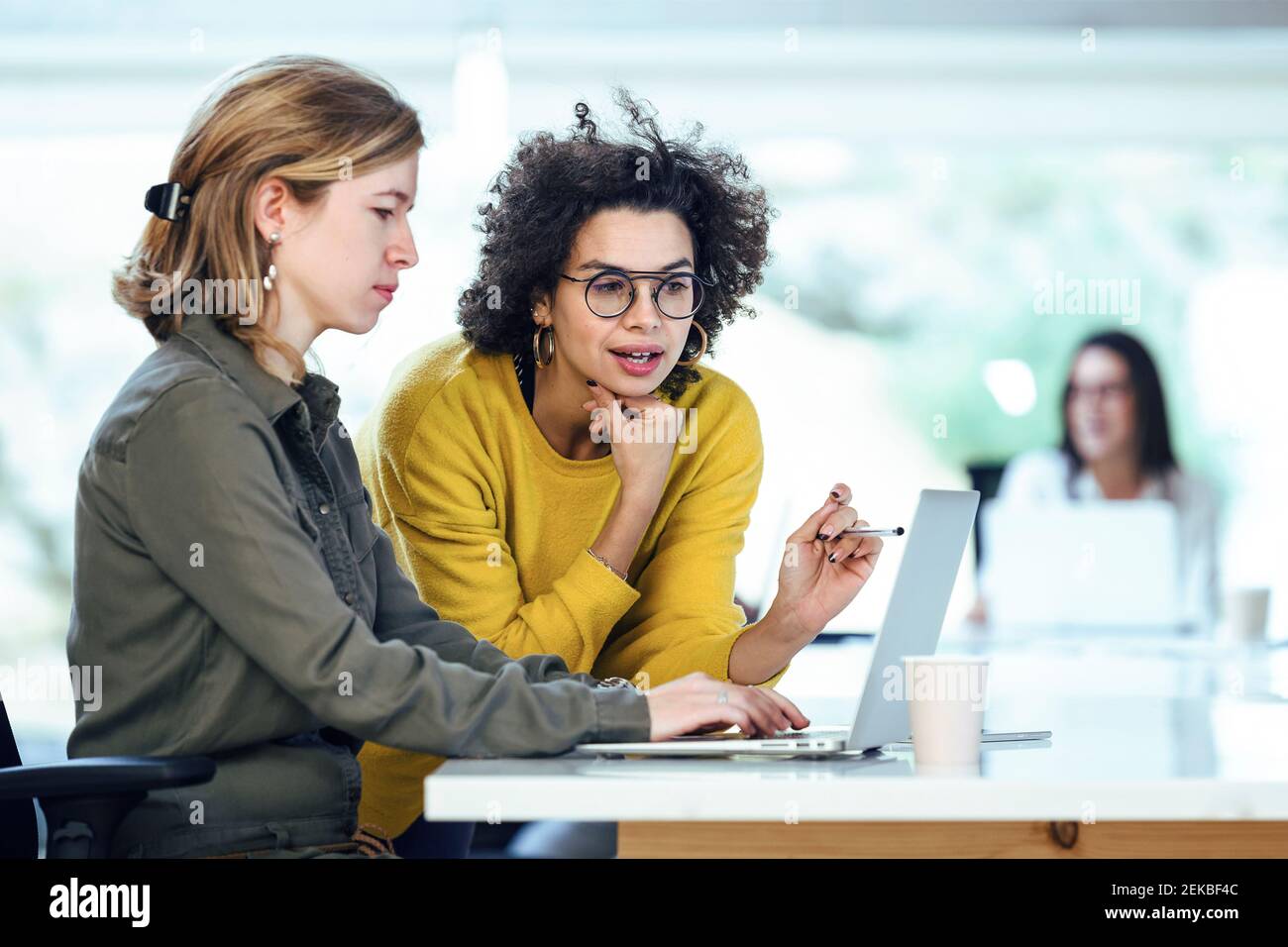 Female colleagues planning strategy while discussing over laptop at ...