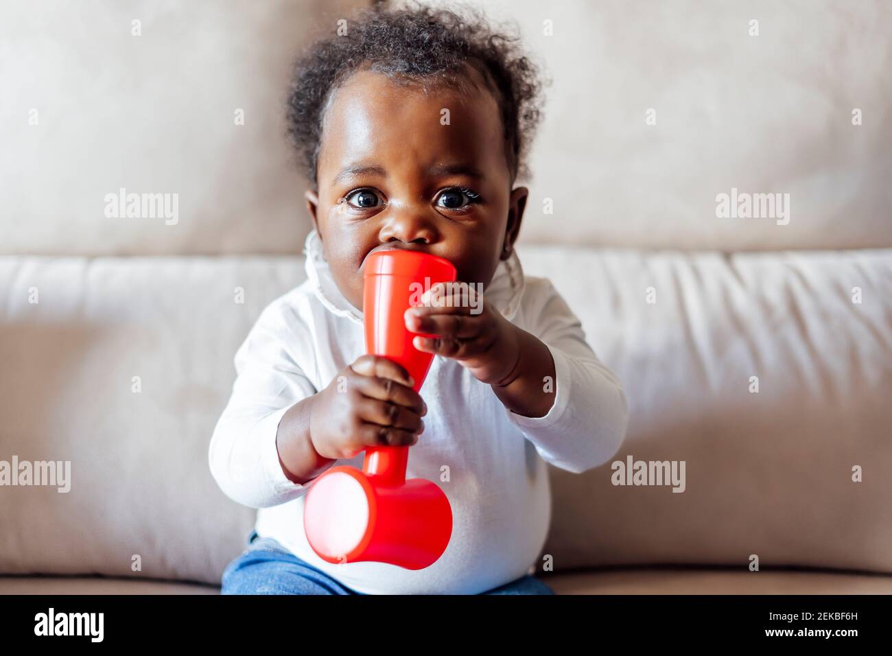 Toddler girl playing with red toy hammer while sitting on sofa at home ...