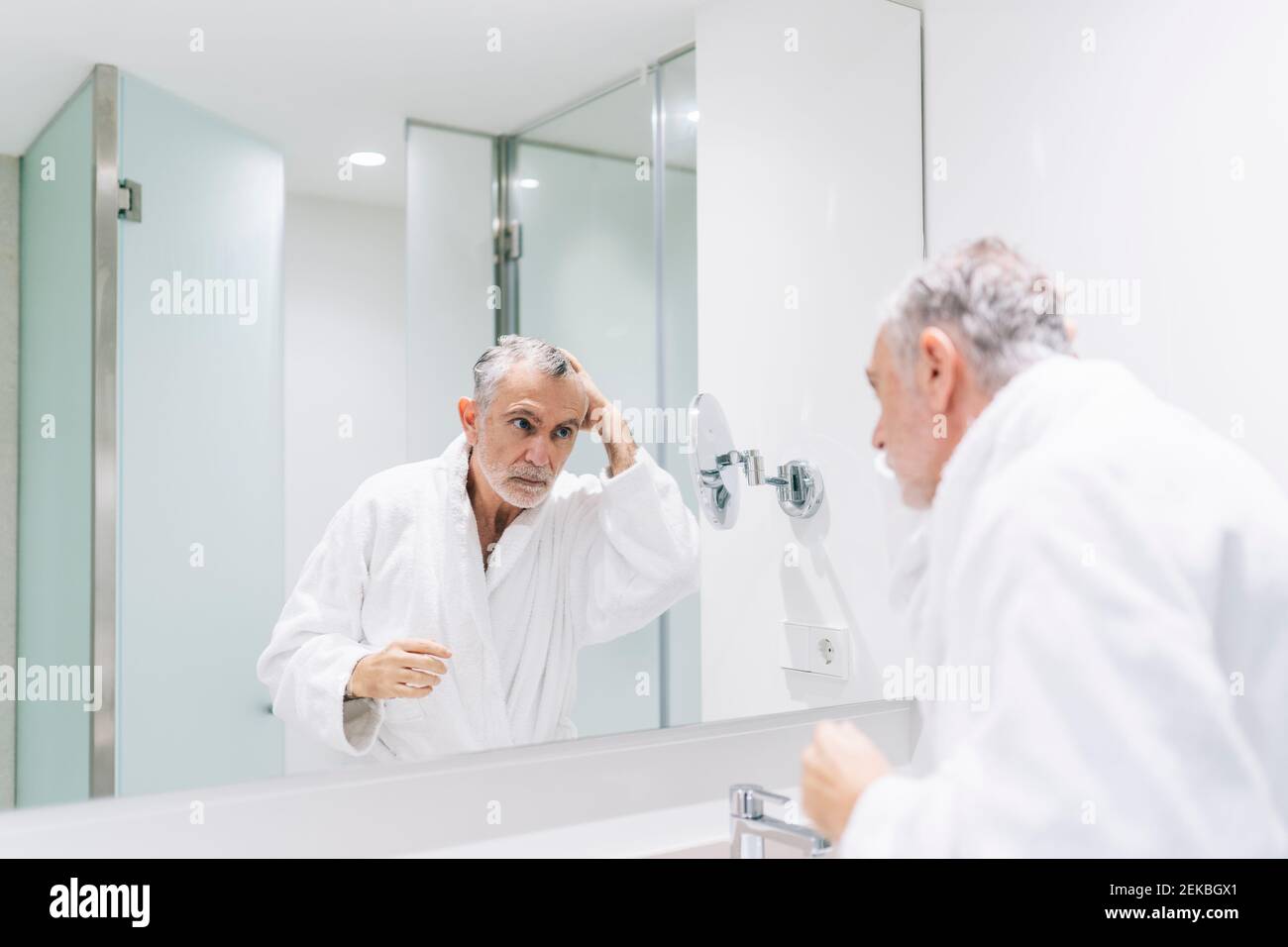 Handsome man looking at reflection in mirror of hotel bathroom Stock ...