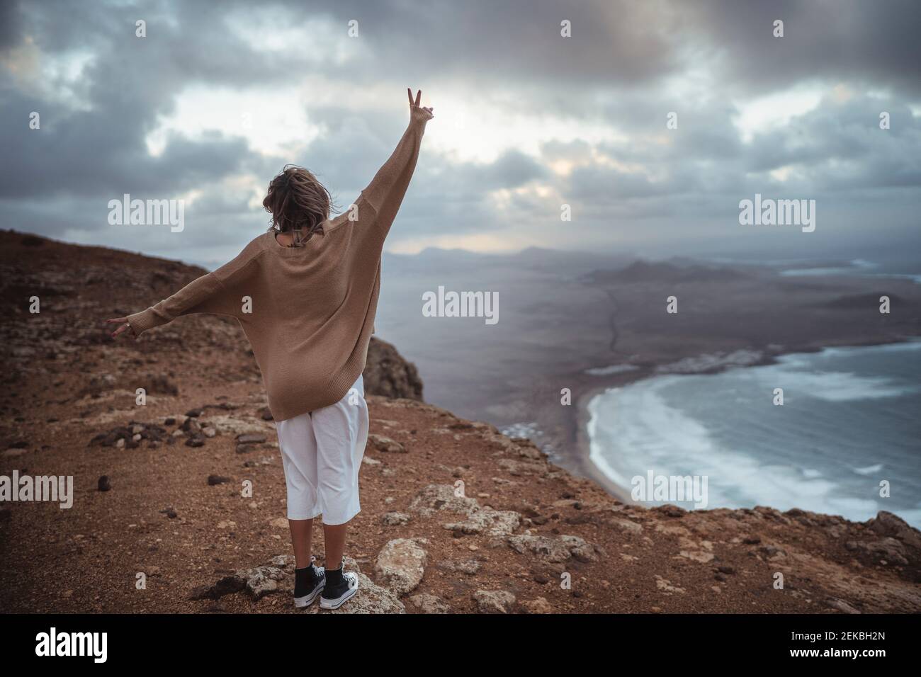 Playful woman gesturing peace sign standing mountain famara beach hi ...