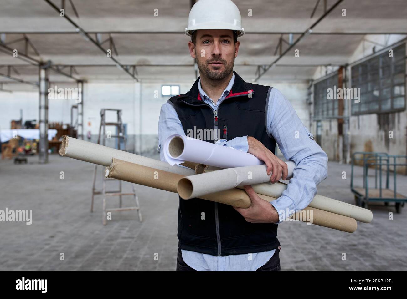 Confident male architect holding cardboards while standing in building ...