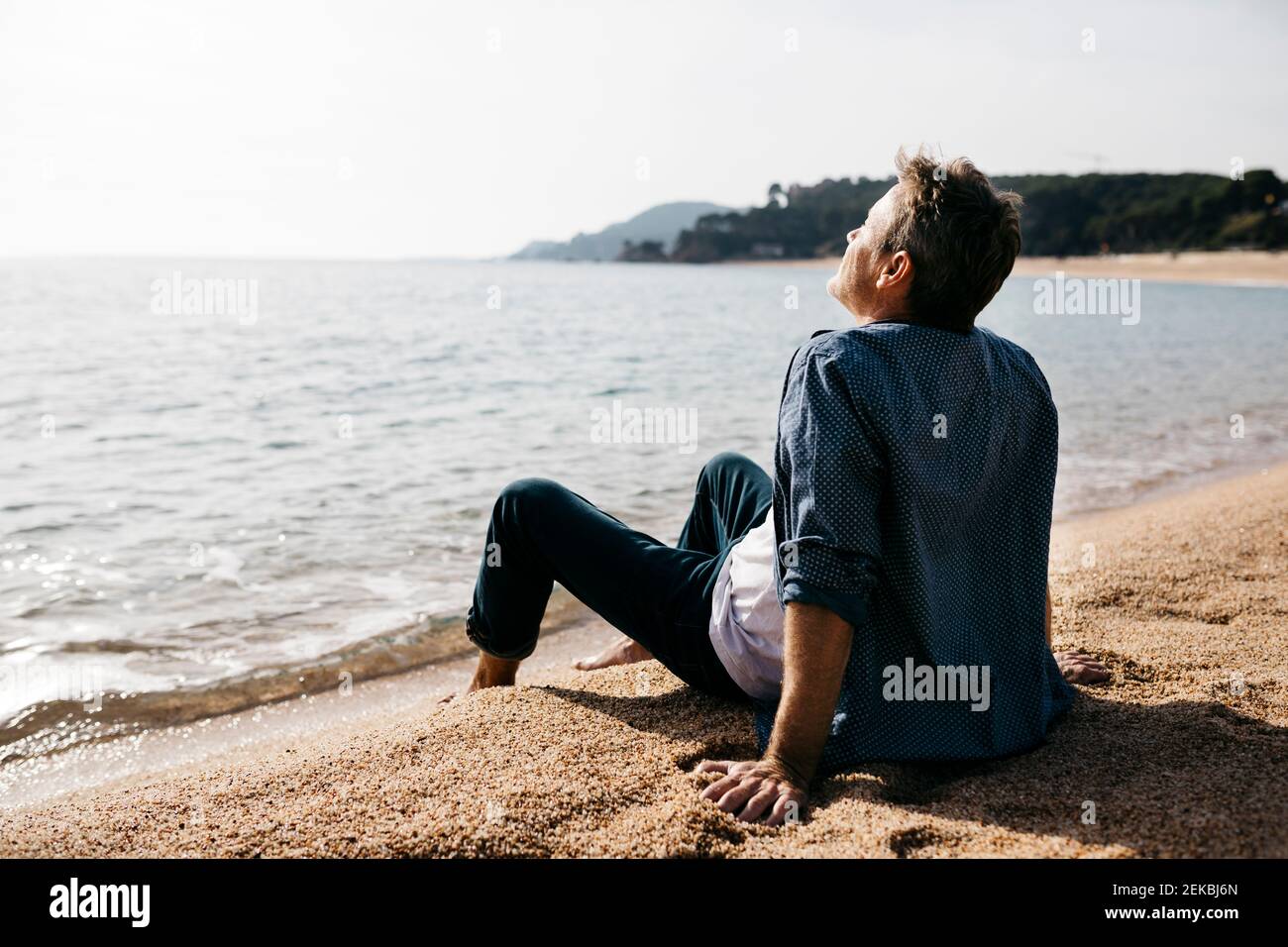 Relaxed man sitting on shore at beach during sunny day Stock Photo - Alamy