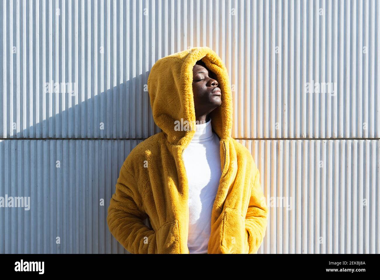 Young African man in yellow jacket with hands in pockets against white ...