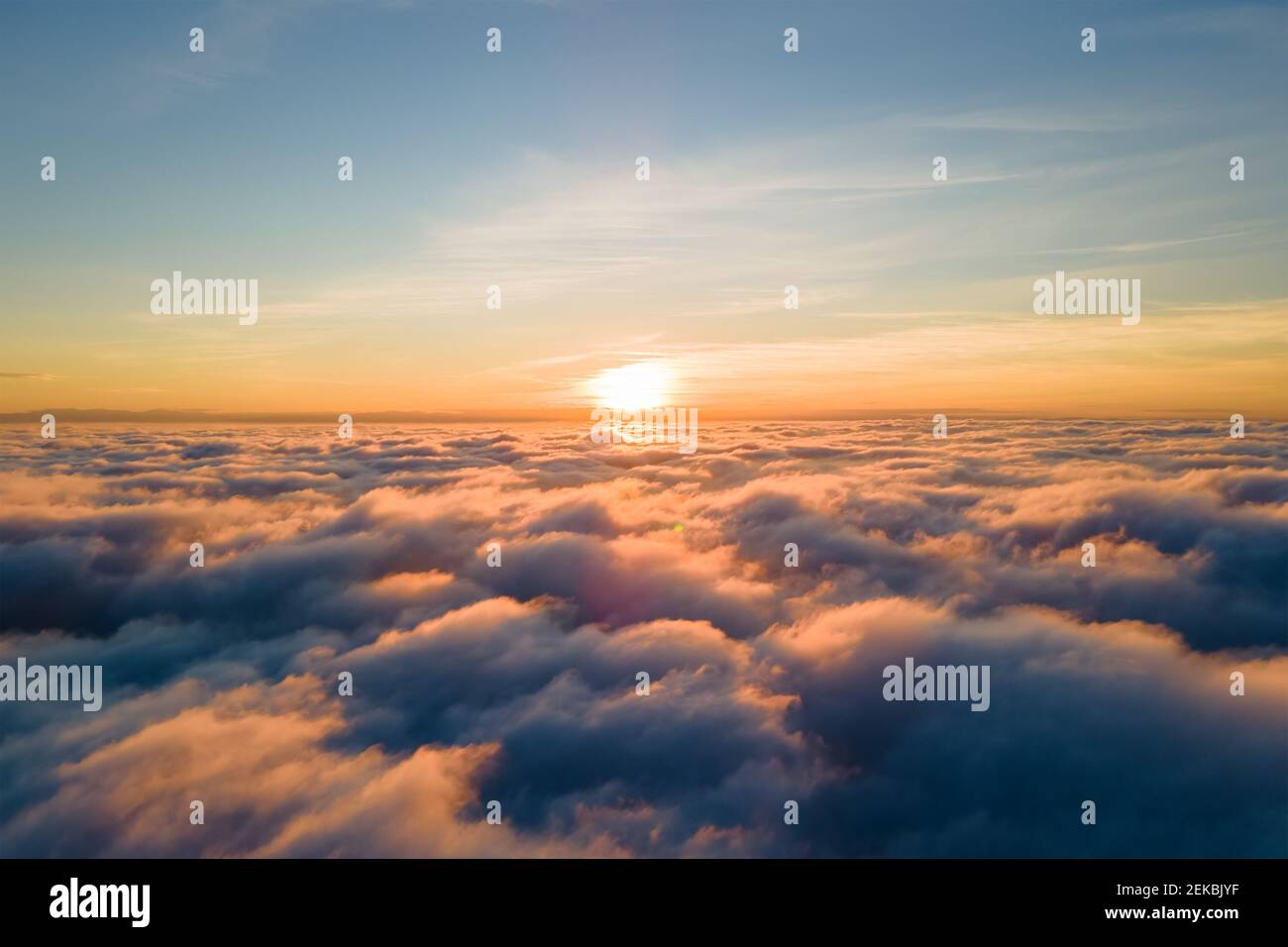Aerial view of bright yellow sunset over white dense clouds with blue ...
