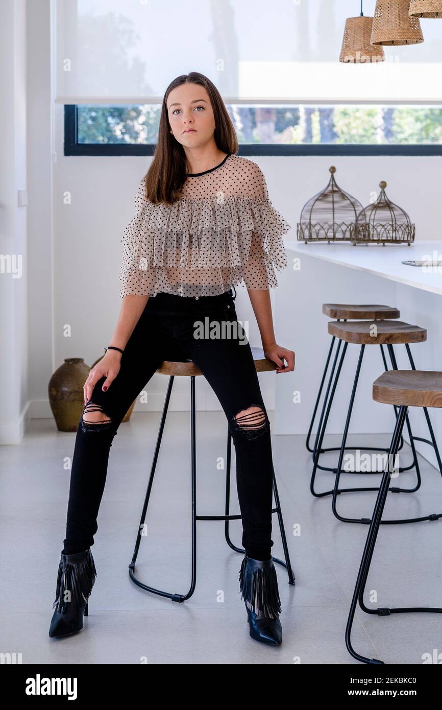 Stylish teenage girl sitting on stool in kitchen at home Stock Photo ...