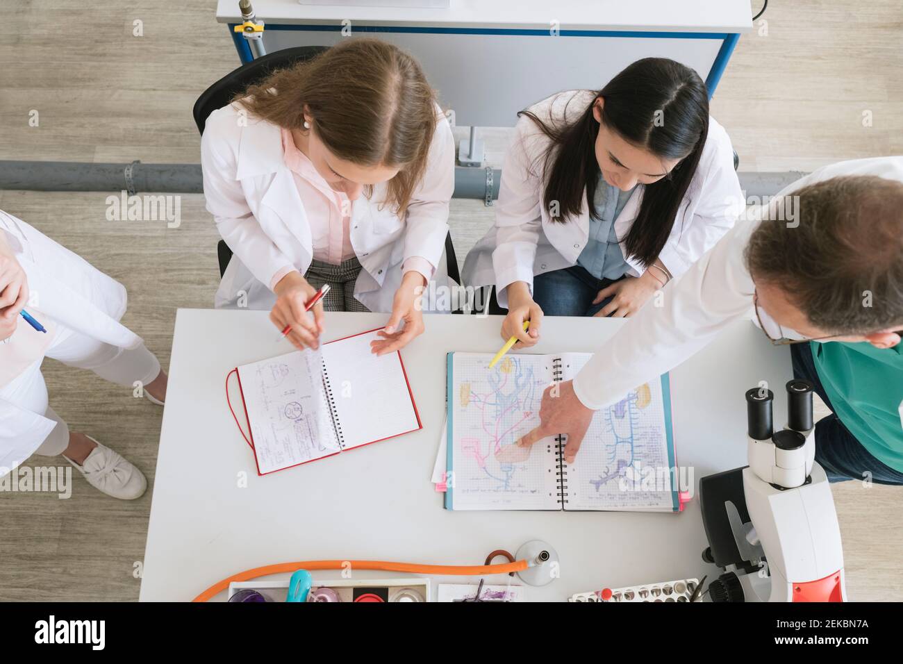 View from above of students and teacher pointing his finger in notebook ...