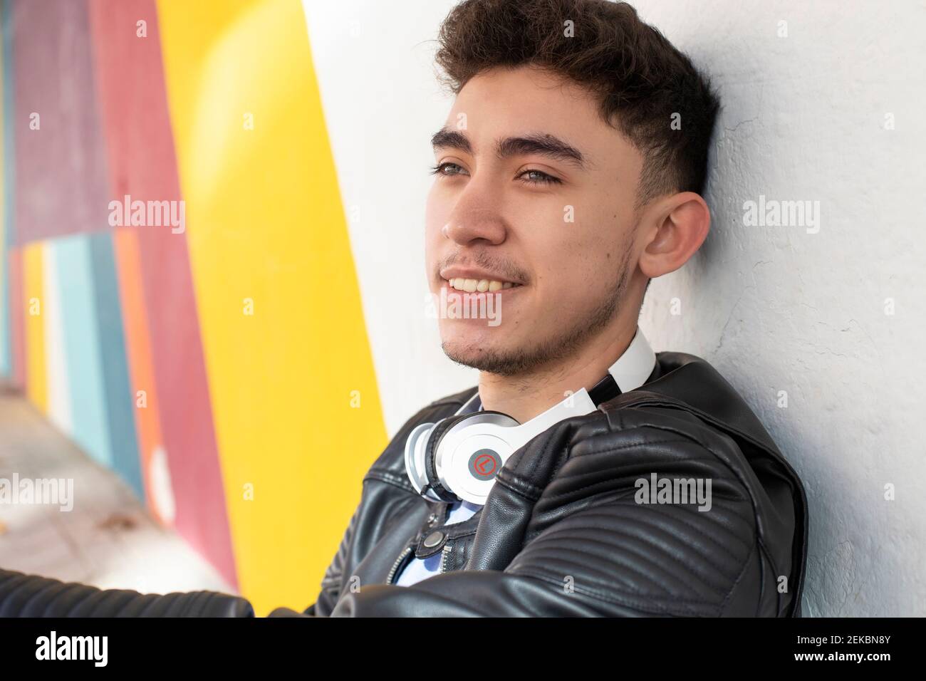 Young man pointing while listening music through headphones against ...