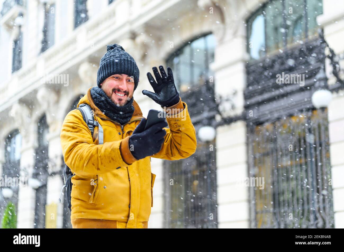 Smiling man waving hand to mobile phone while talking on video call by ...