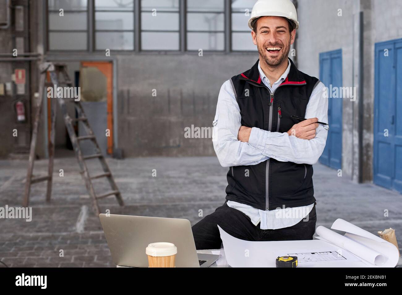 Male architect with arms crossed laughing while standing at table in ...