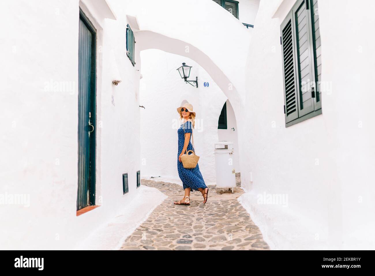 Woman wearing hat walking at alley amidst houses in Binibeca village ...