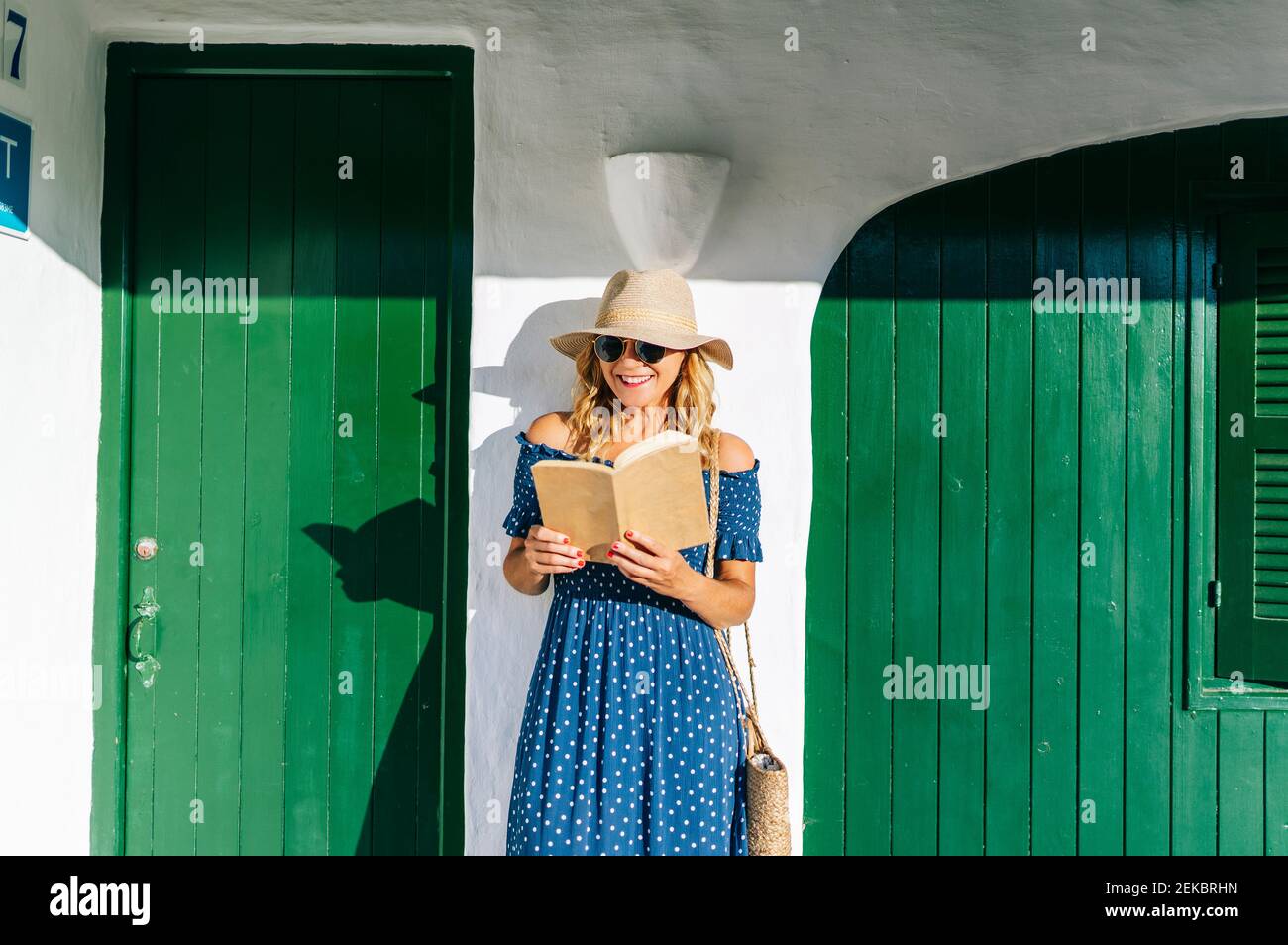 Mature woman wearing hat reading book while standing against house in ...
