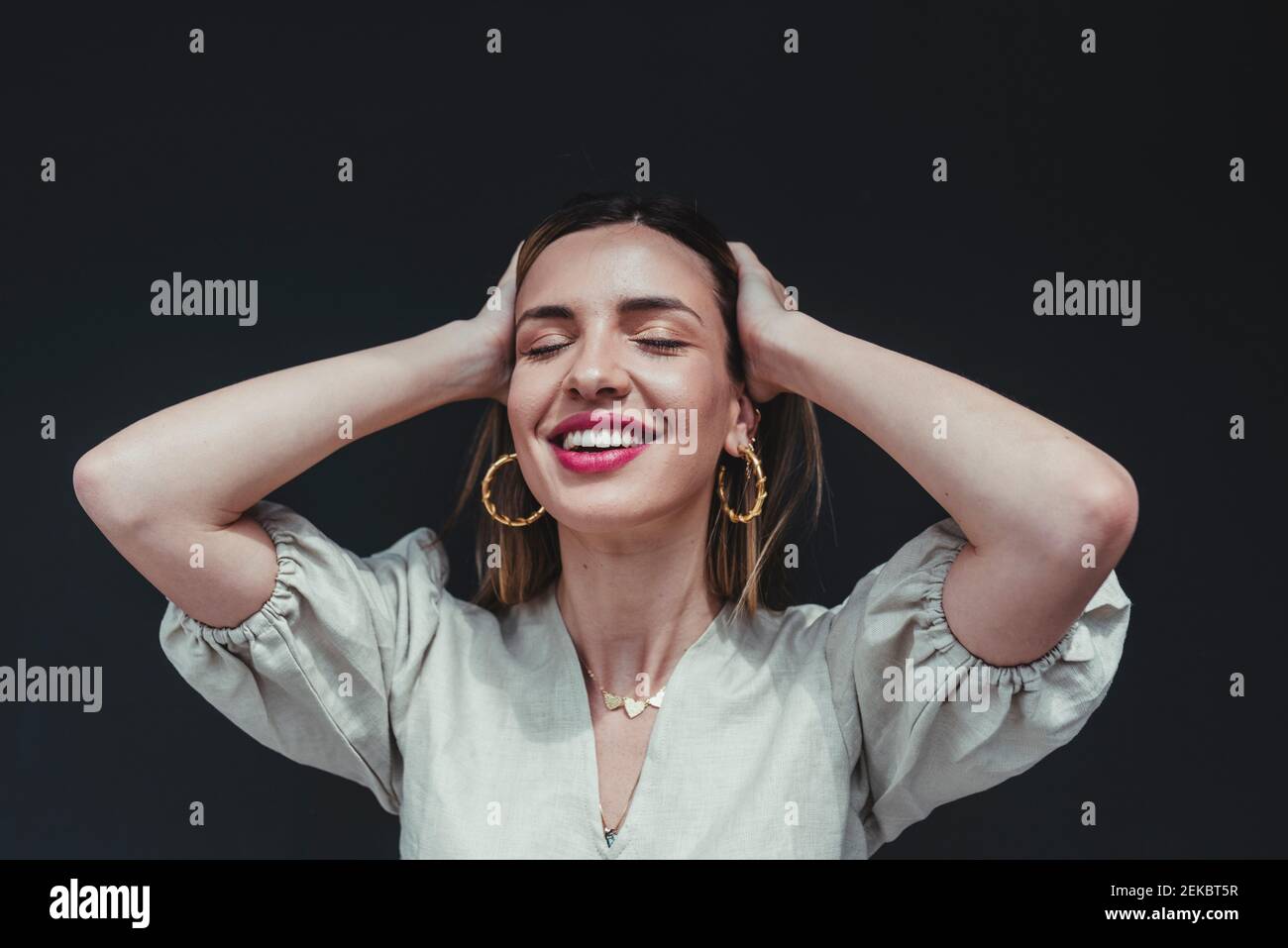 Cheerful mid adult woman with hands in hair against black background ...