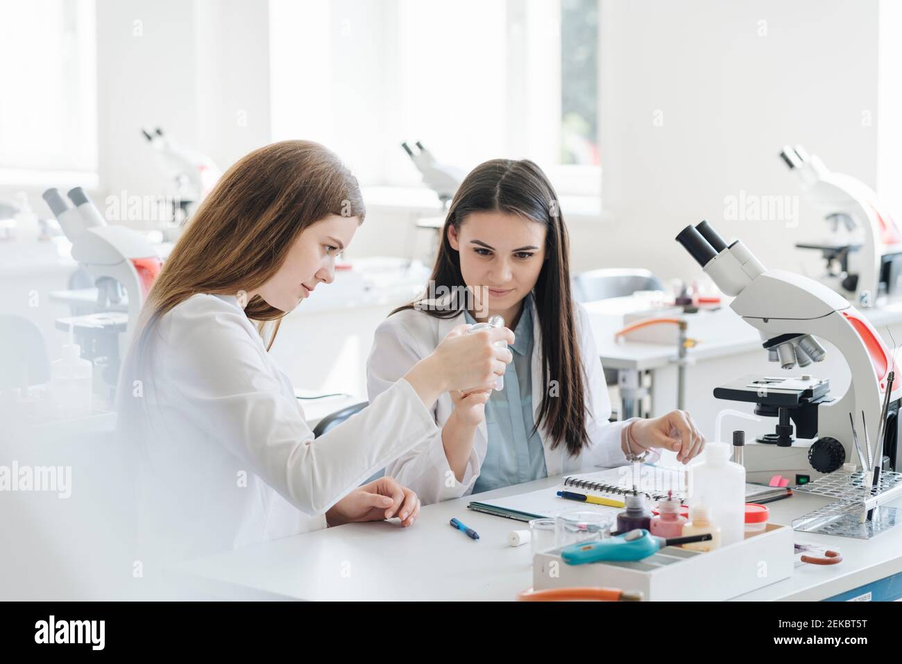 Young female researchers in white coats examining laboratory sample in ...