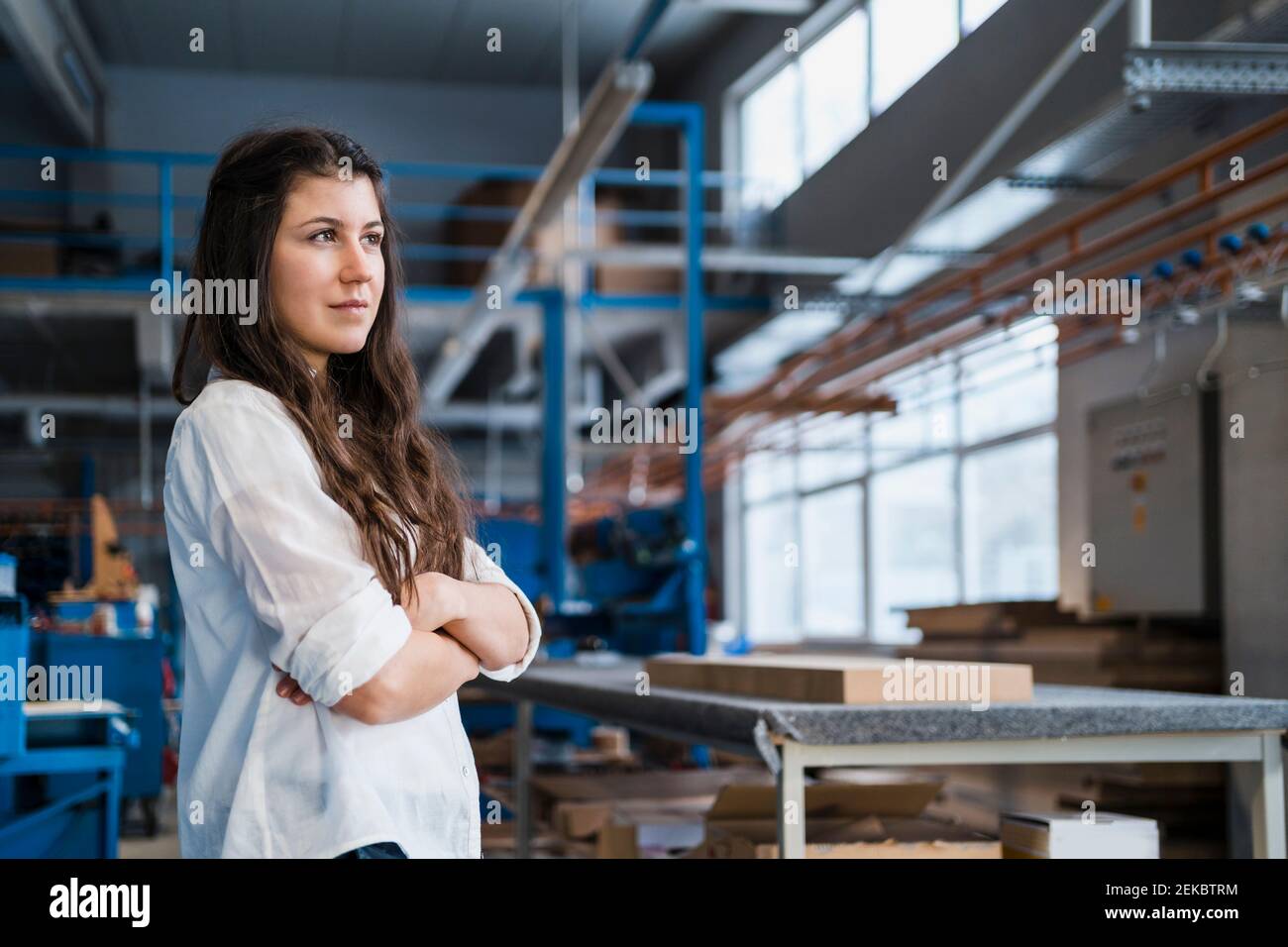 Confident female expertise with arms crossed looking away while standing at industry Stock Photo ...