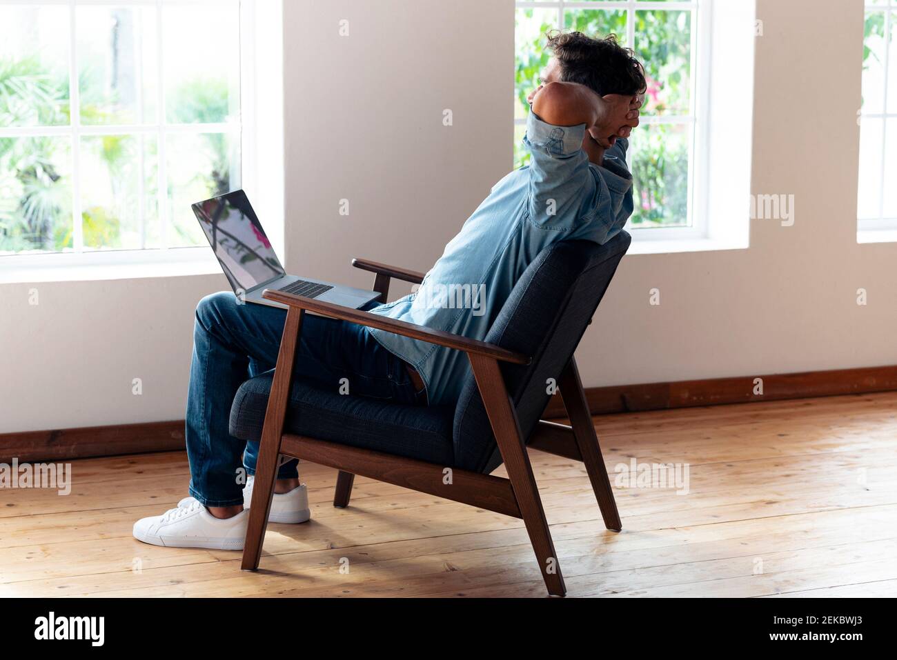 Man with hands behind head resting while sitting on armchair at home ...