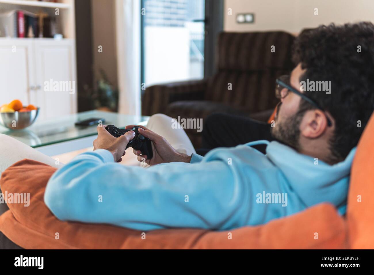 Relaxed young man playing video game while sitting on sofa in living ...