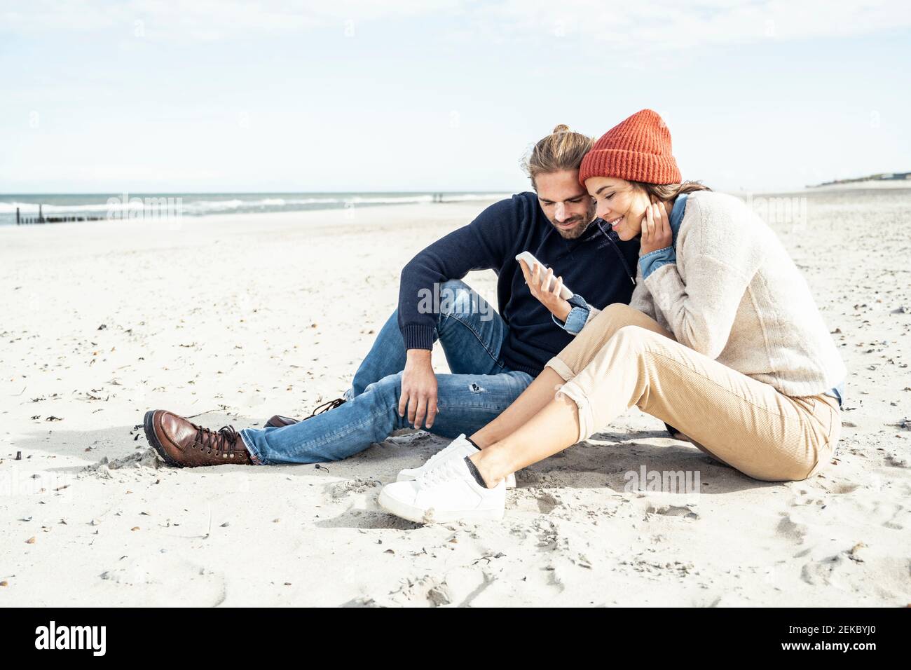 Young couple sitting together on beach sand and using smart phone Stock ...