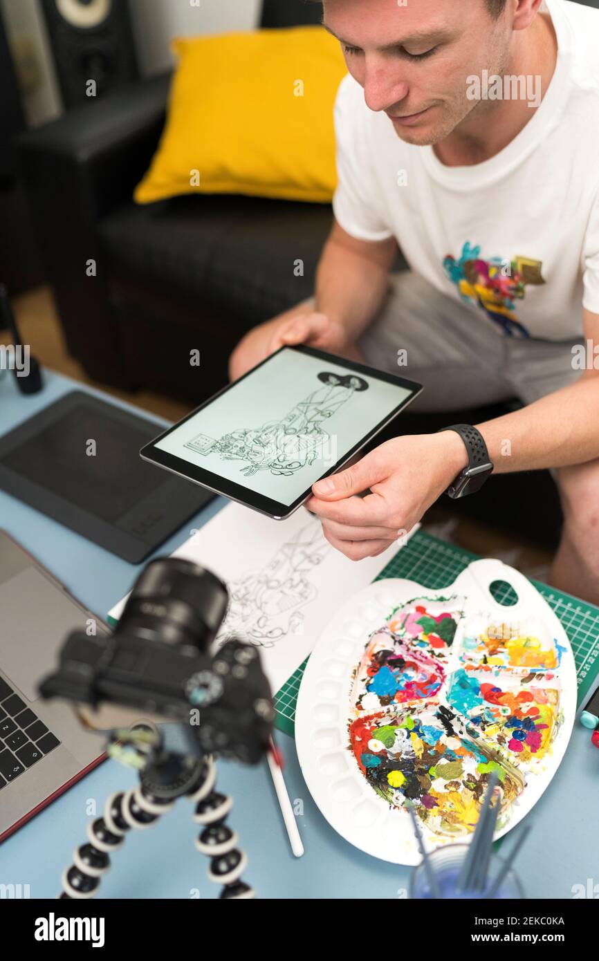 Artist looking at digital tablet while live streaming through laptop ...