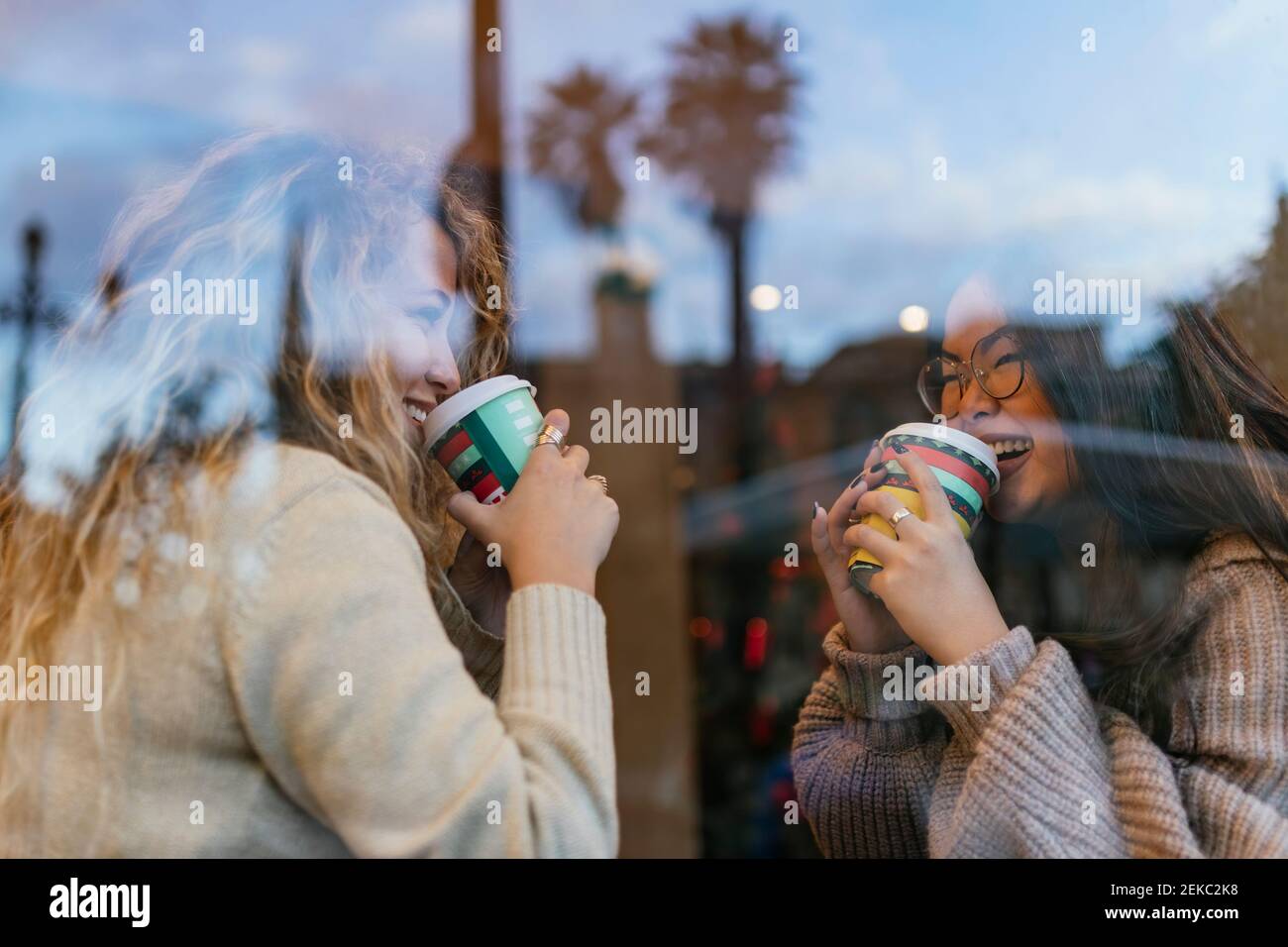 Cheerful female friends having coffee in cafe seen through glass window ...