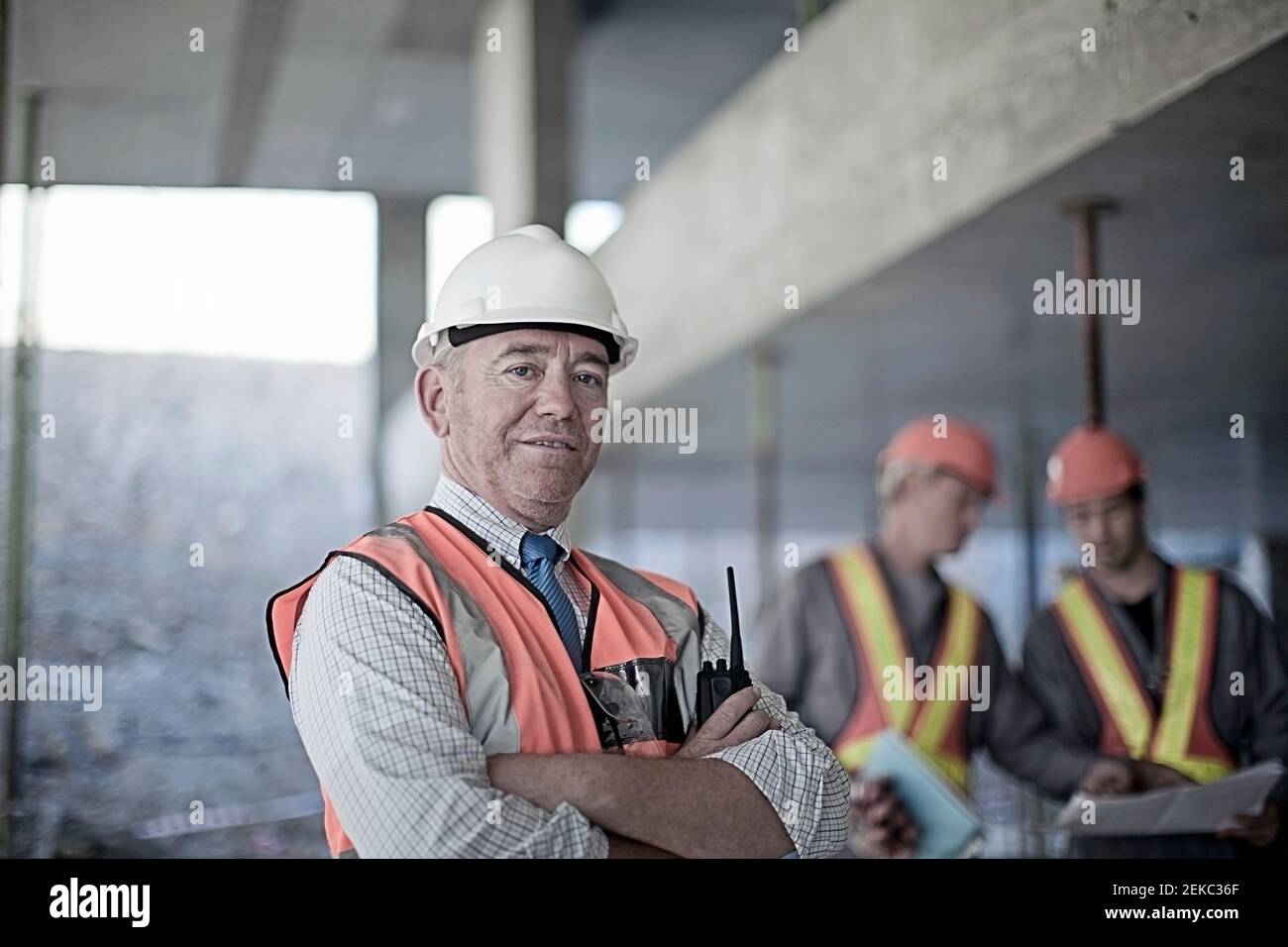 Confident male contractor with arms crossed at site with construction ...