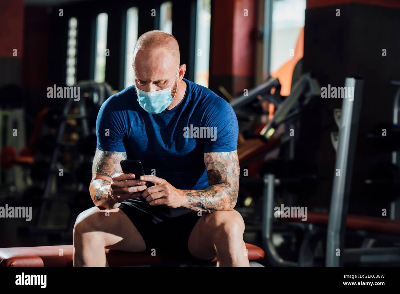 Man wearing face mask using mobile phone while sitting in gym during ...