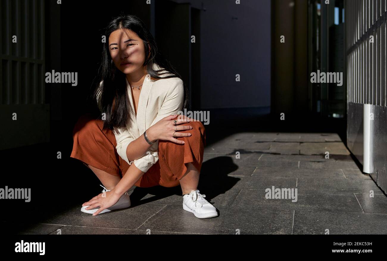 Young woman crouching by gate with hand shadow on face Stock Photo - Alamy