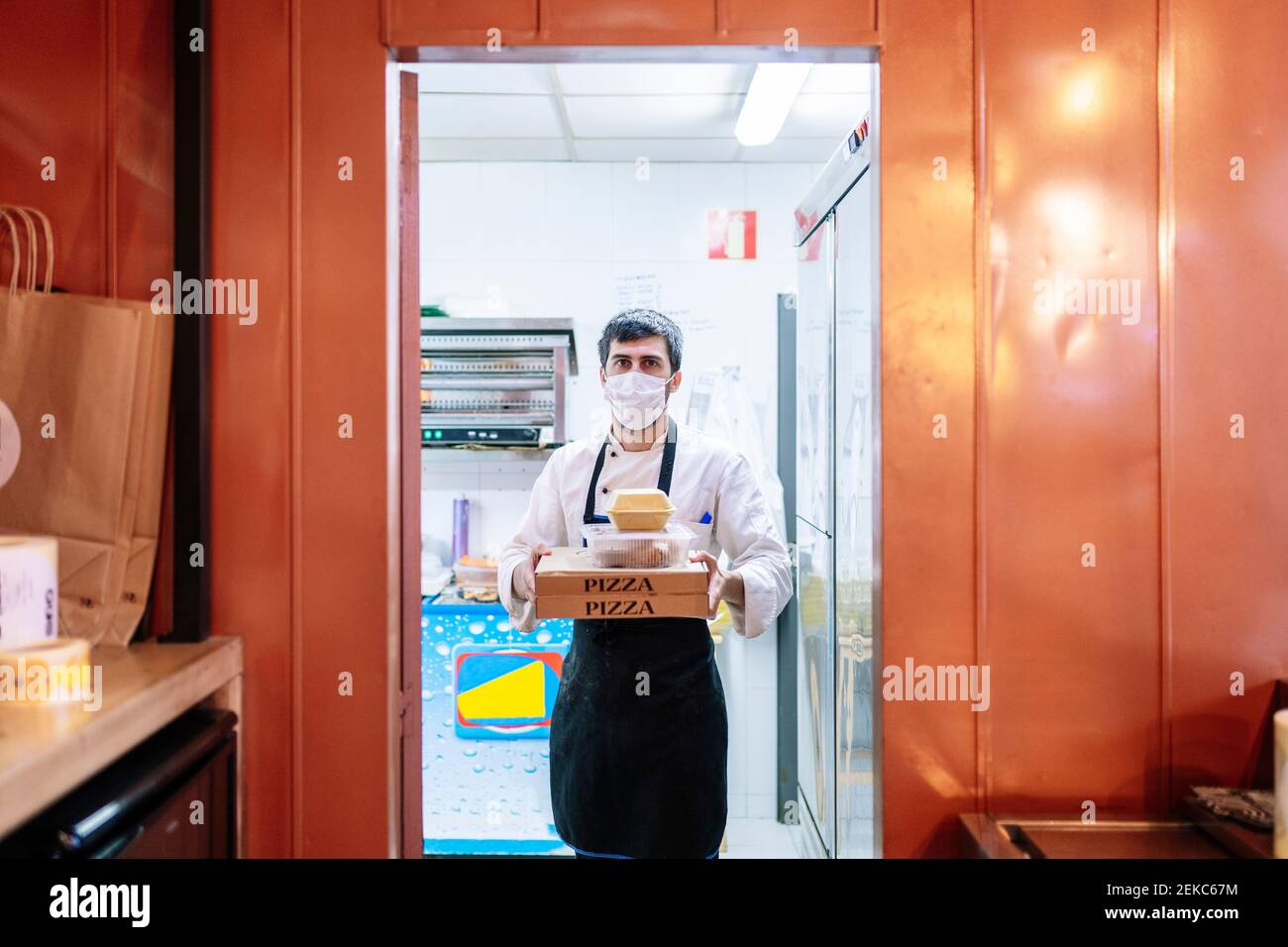 Male chef carrying pizza boxes and food container while working in ...