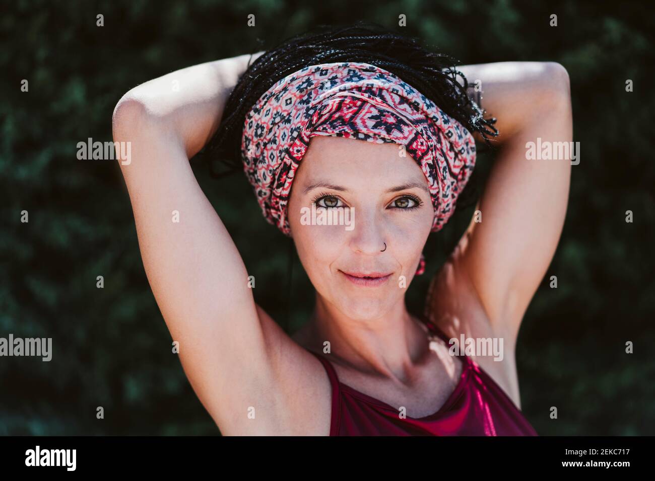Beautiful woman staring while standing with hands behind head outdoors ...