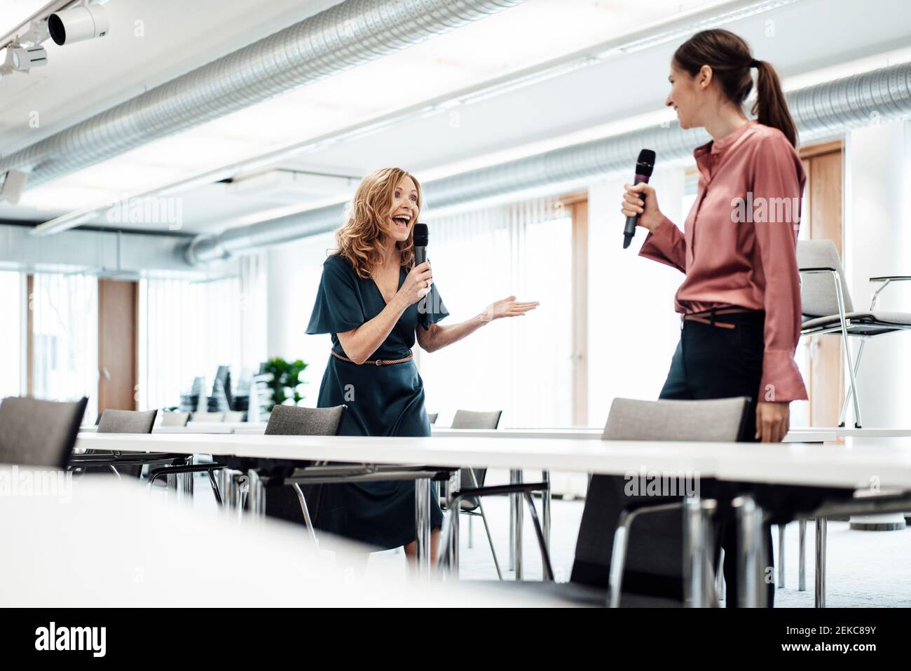 Cheerful female colleagues singing on microphone at conference table ...