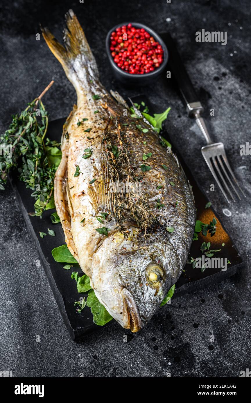 Roasted sea bream fish with herbs on a cutting board. Black background ...